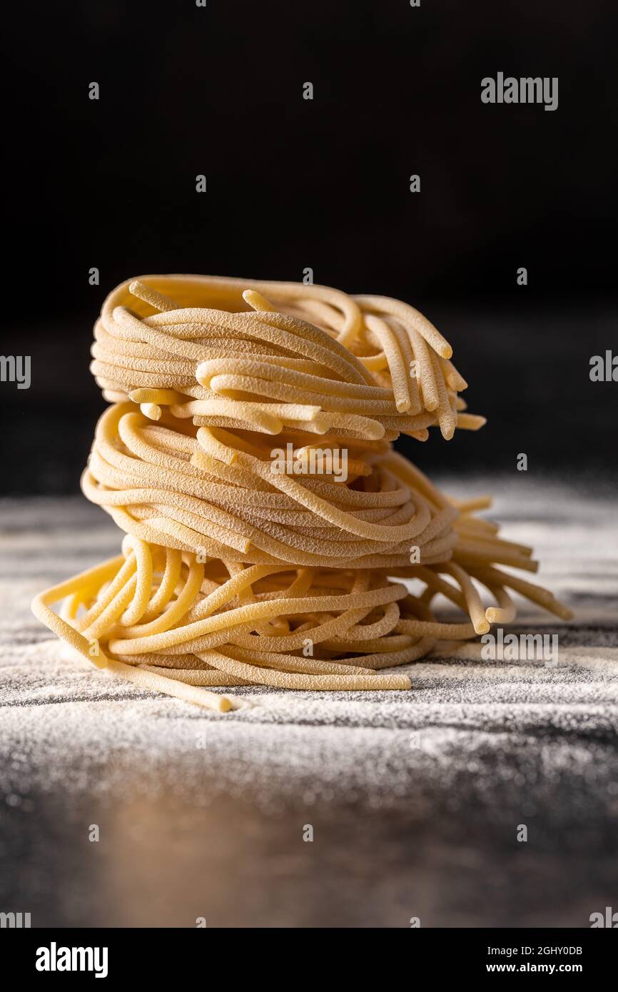 Italian pasta nest. Uncooked spaghetti nest and flour on black table ...