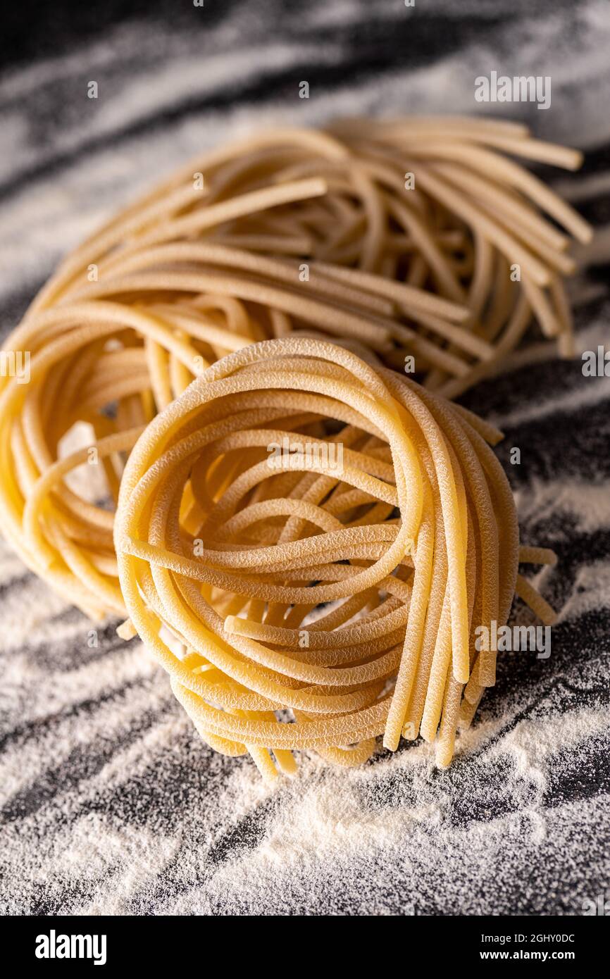 Italian pasta nest. Uncooked spaghetti nest and flour on black table ...