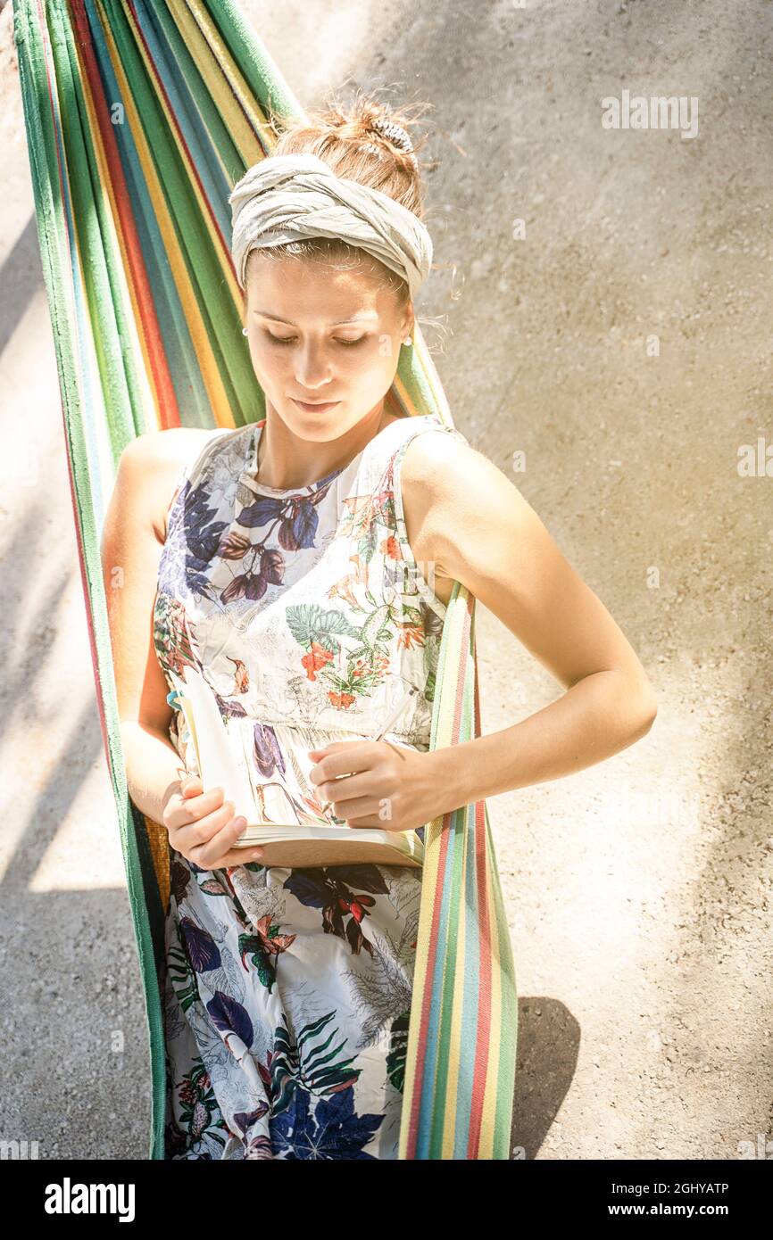vertical photograph of a woman in a hammock focused writing a diary ...