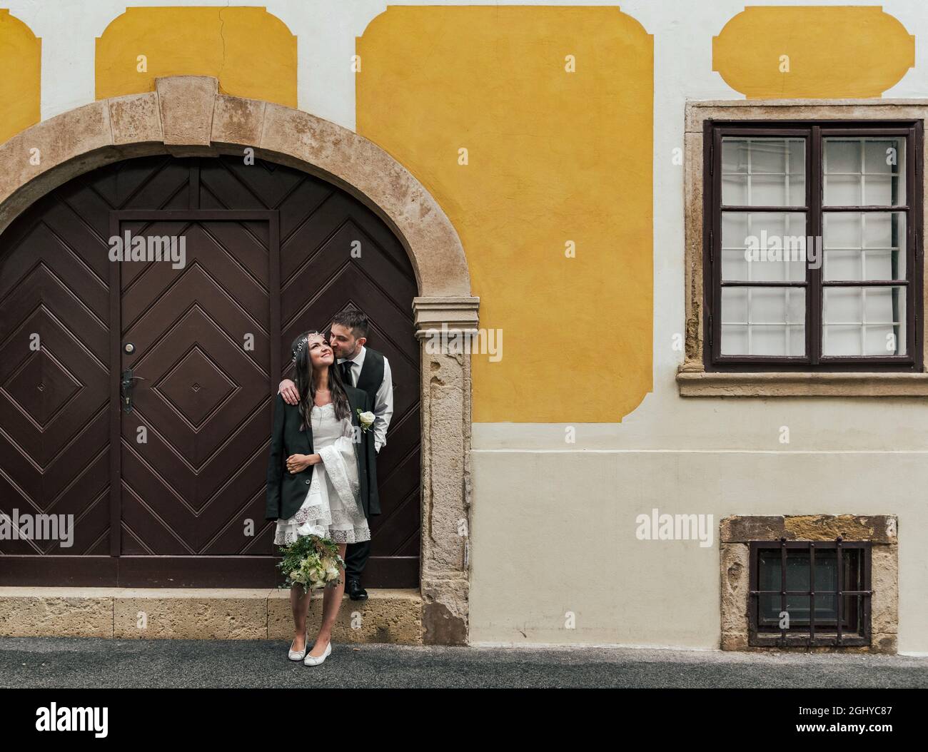 Full length photo of bride and groom standing in front of wooden door ...