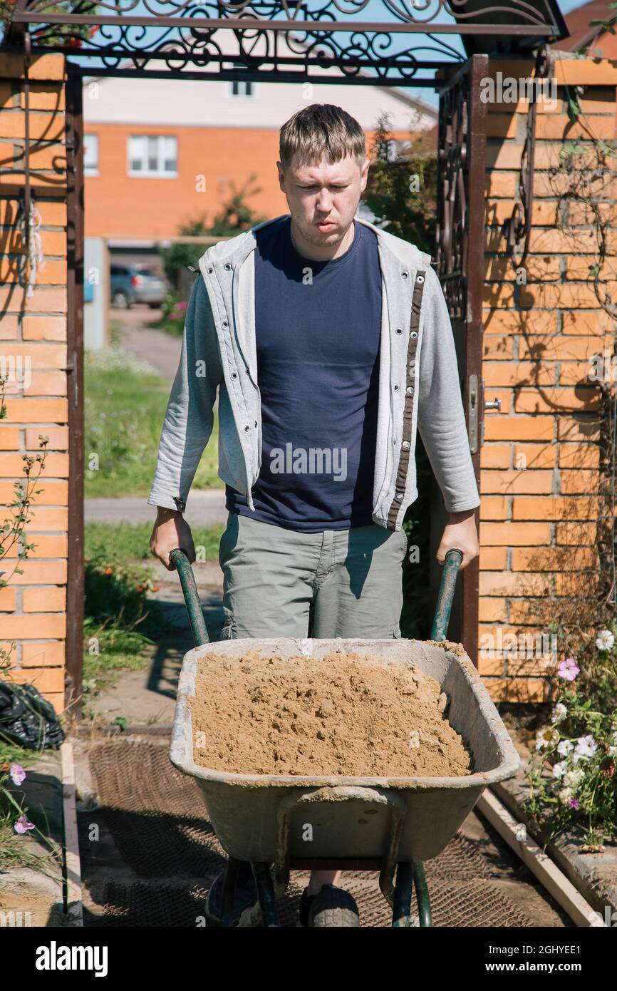 A man unloads sand into a cement mixture for pouring a garden path ...