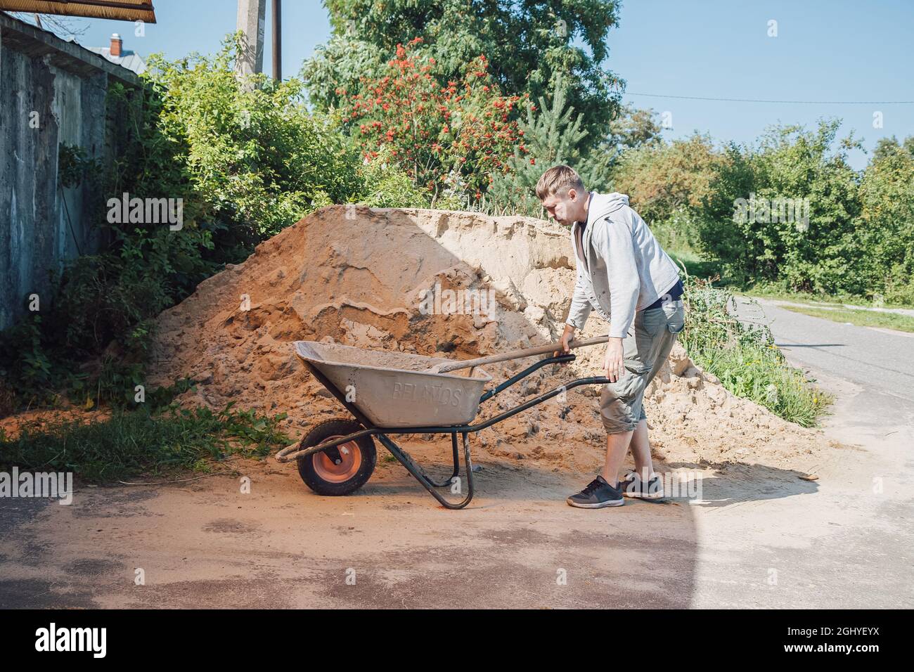 A 30-year-old caucasian man pours sand from a large pile of sand onto a ...