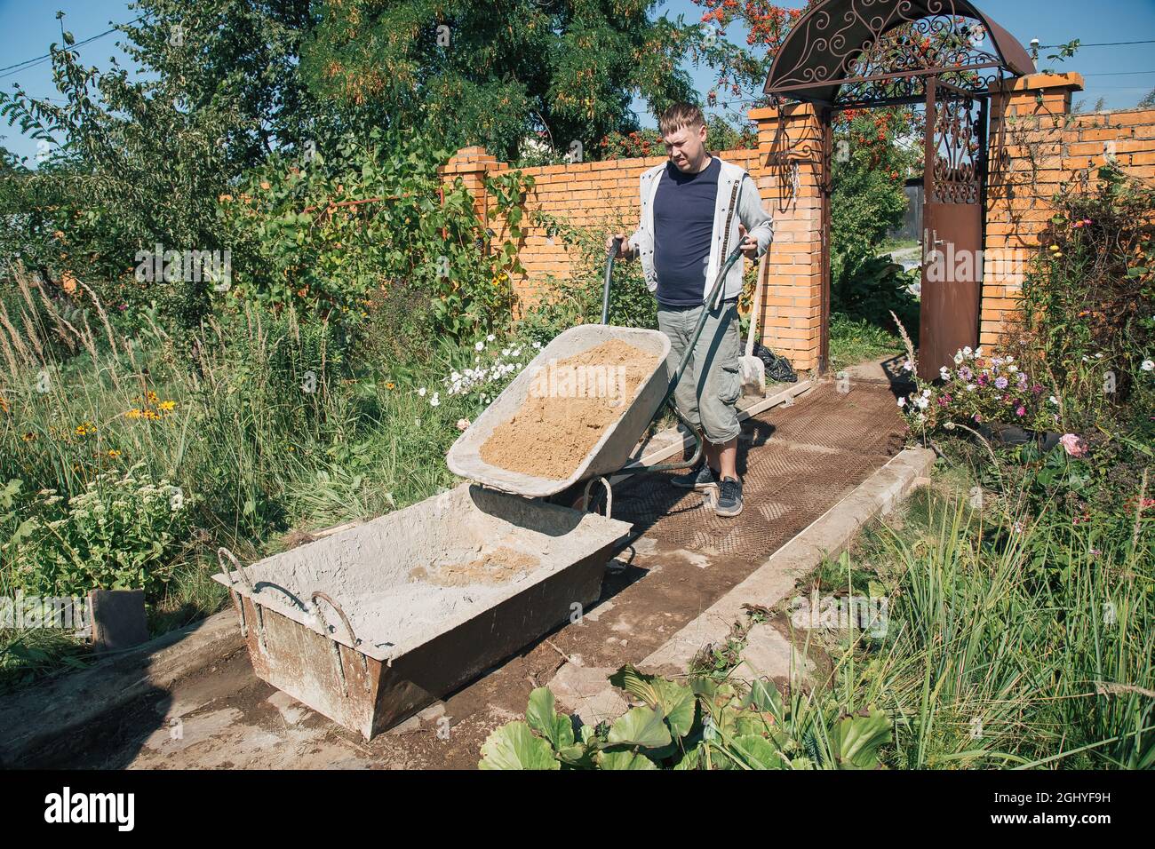 A man unloads sand into a cement mixture for pouring a garden path ...