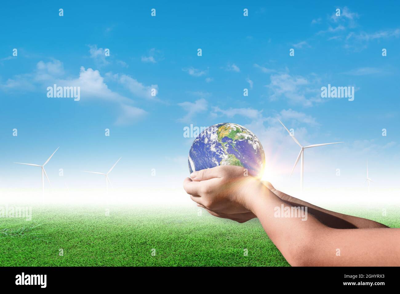 Hands holding earth, globe on wind turbine field against blue sky ...