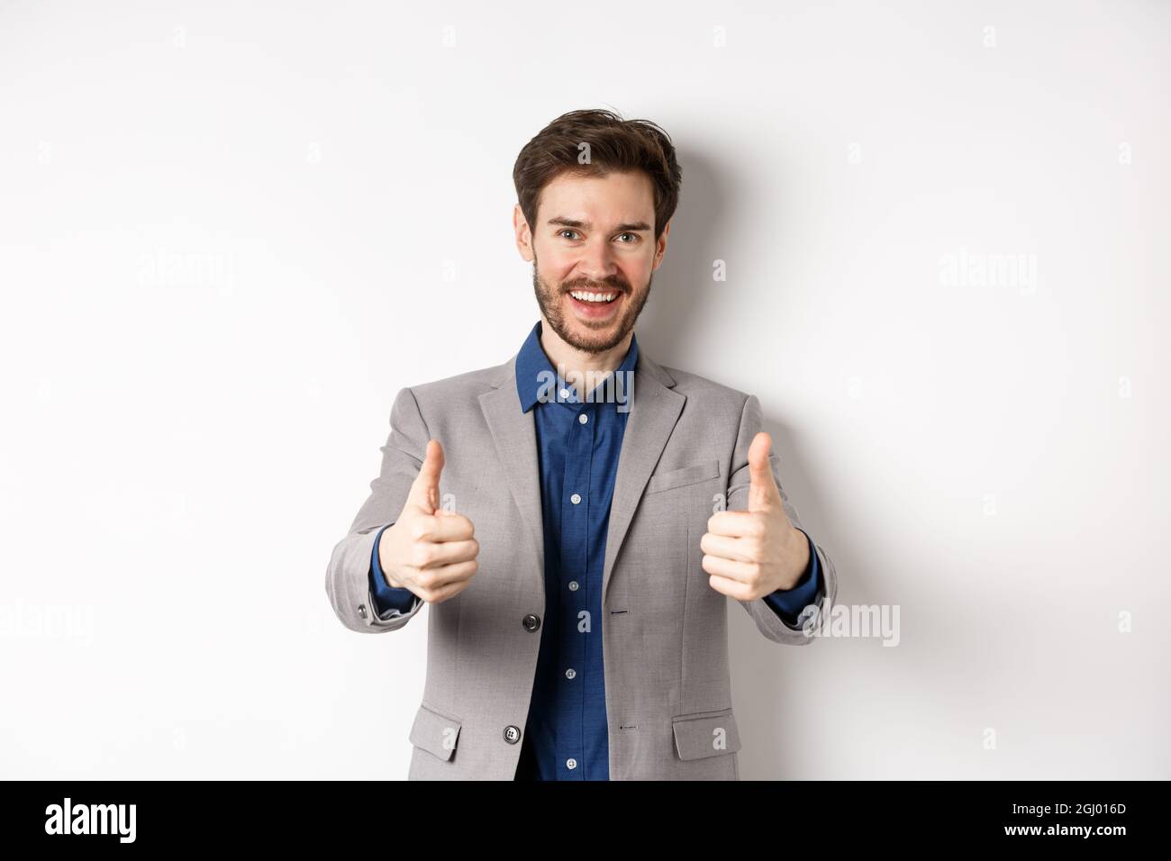 Cheerful and positive young man in business suit showing thumbs up and ...