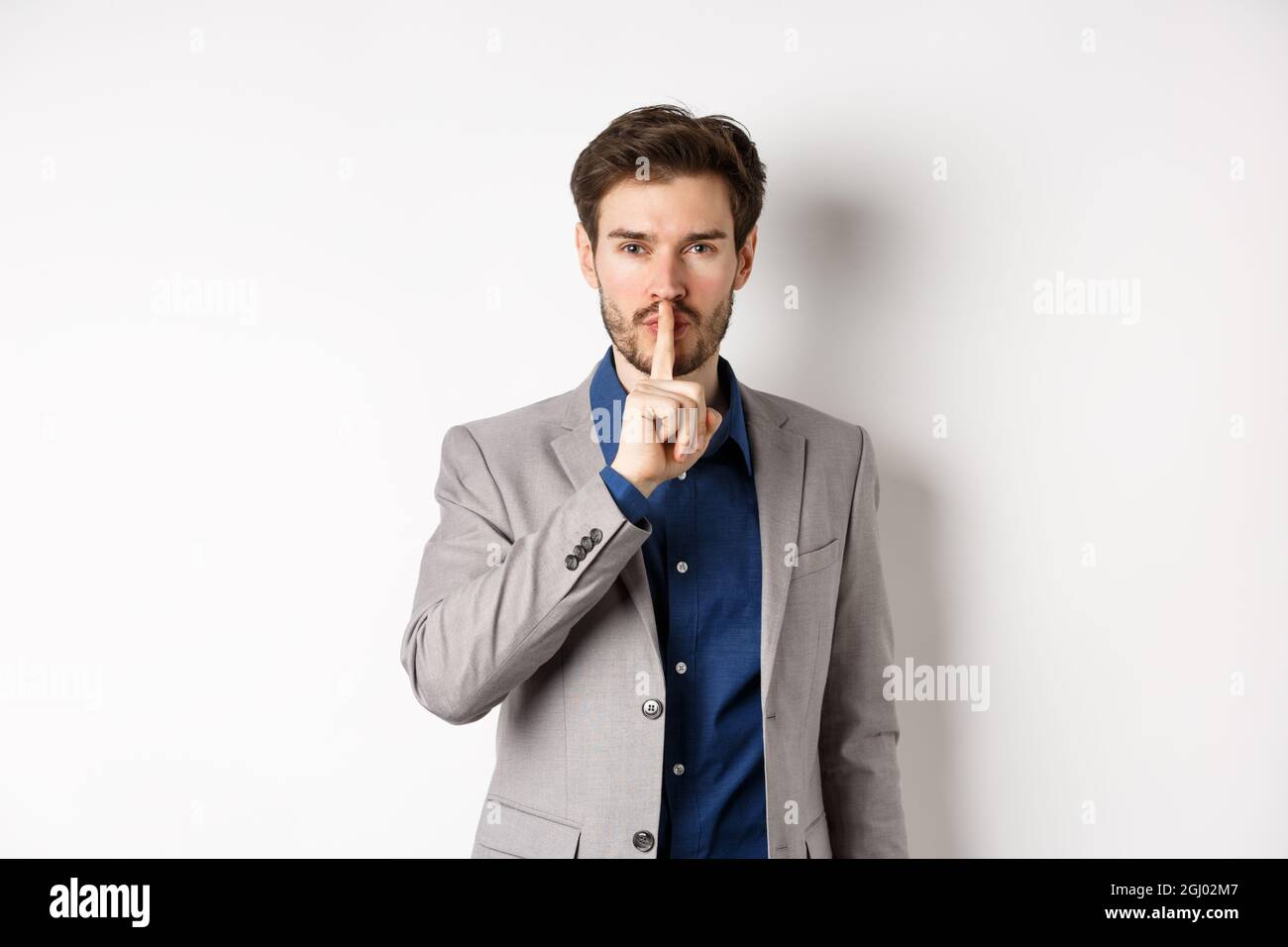 Handsome macho man in suit shushing at camera, press finger to lips ...