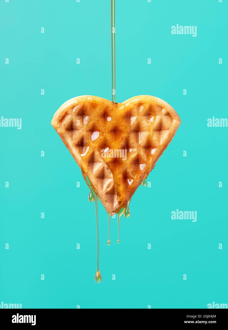 Pouring maple syrup over one heart-shaped waffle against a green ...