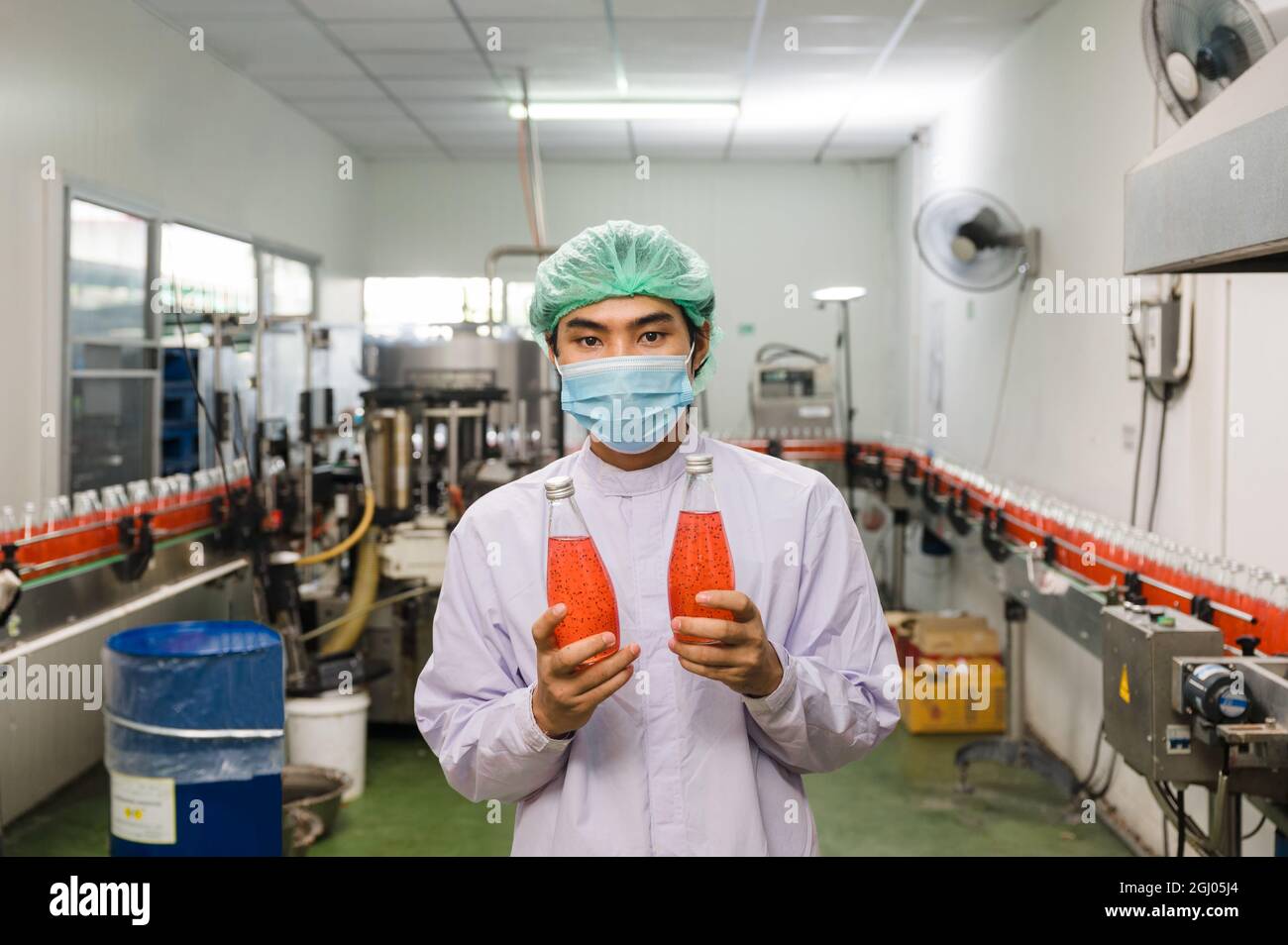Young asian man worker in sterile uniform showing product of bottled ...