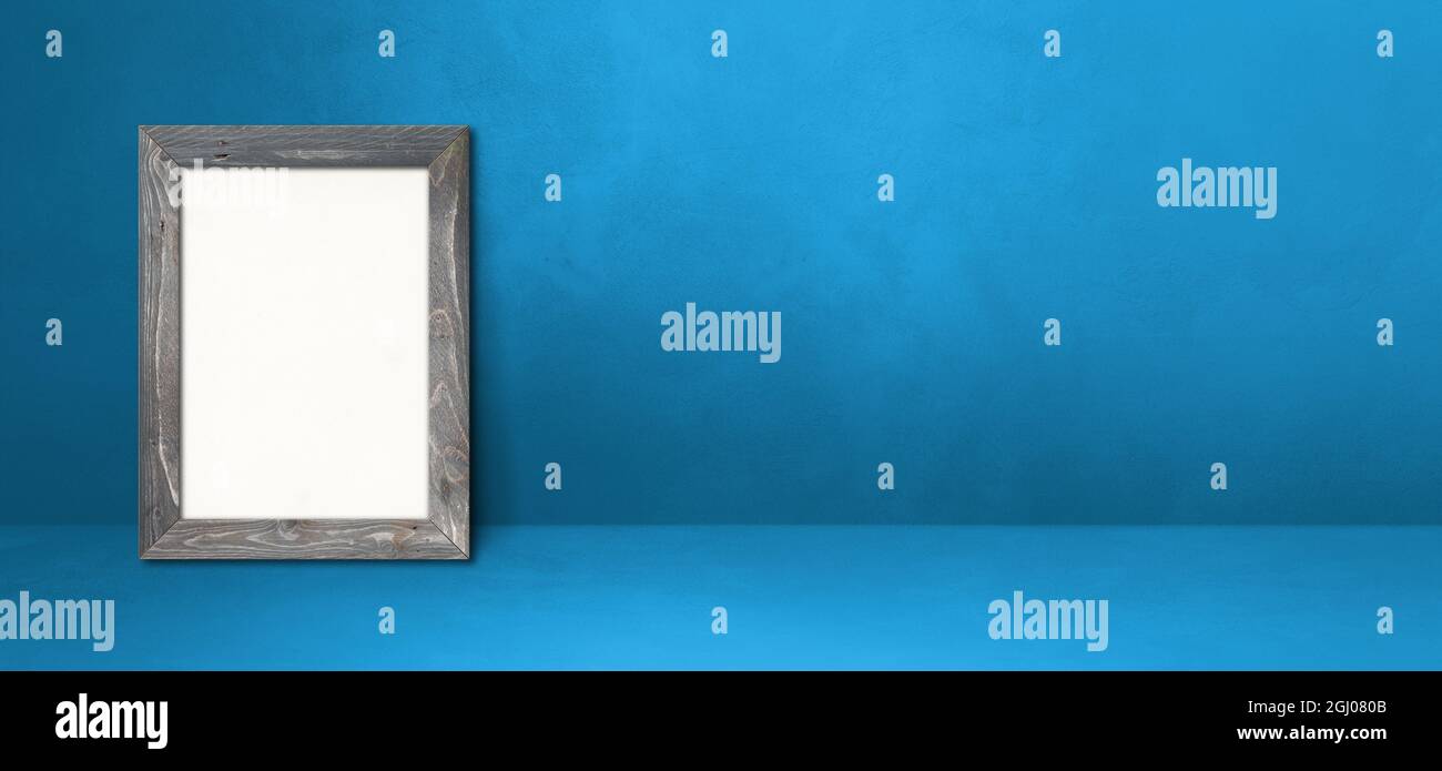 Wooden picture frame leaning on a blue wall. Blank mockup template ...