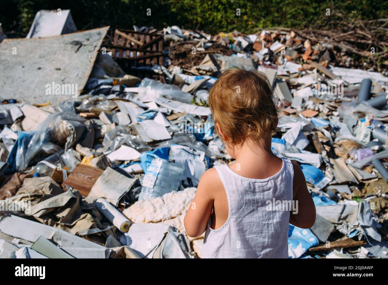 Little girl at a dump among a heap of scattered garbage in the forest ...