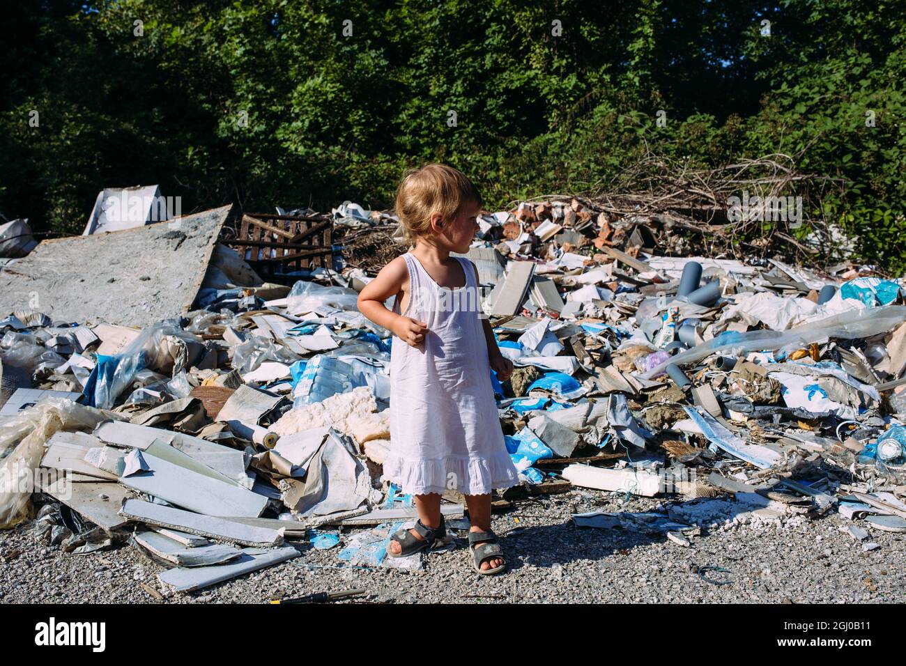 Little girl at a dump among a heap of scattered garbage in the forest ...