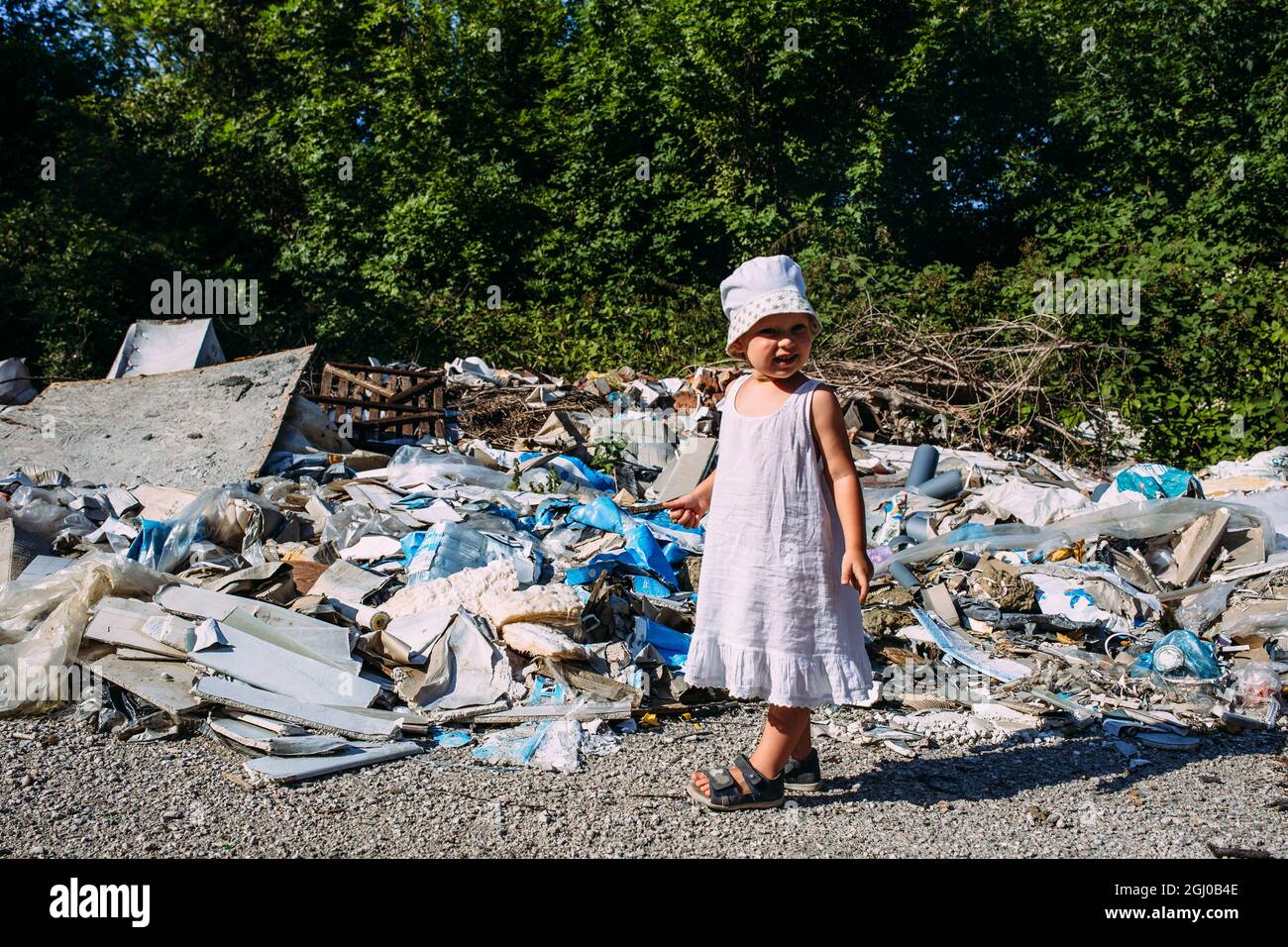 Little girl at a dump among a heap of scattered garbage in the forest ...