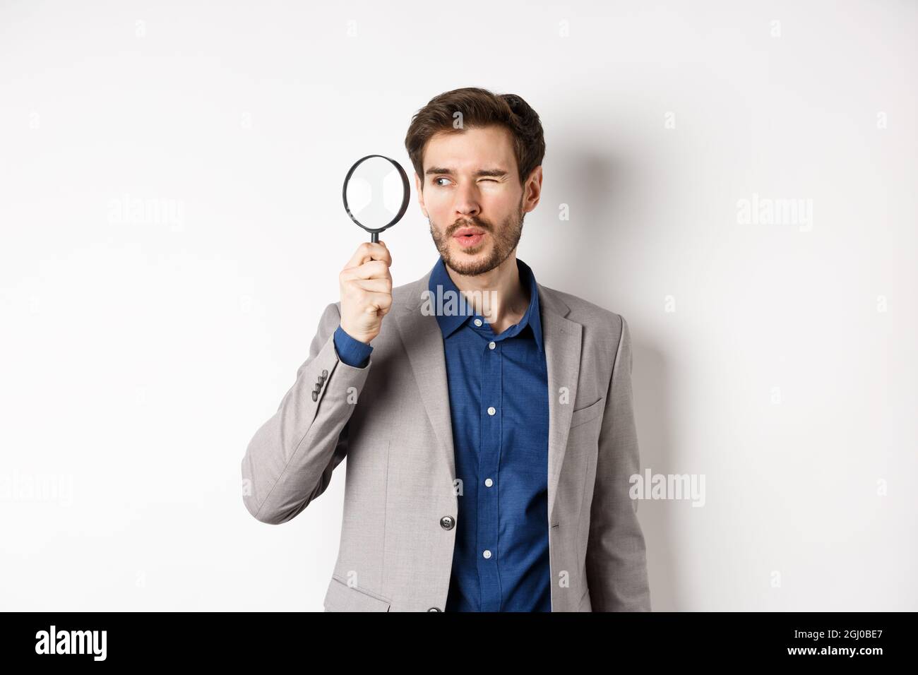 Handsome male model in suit looking through magnifying glass with ...