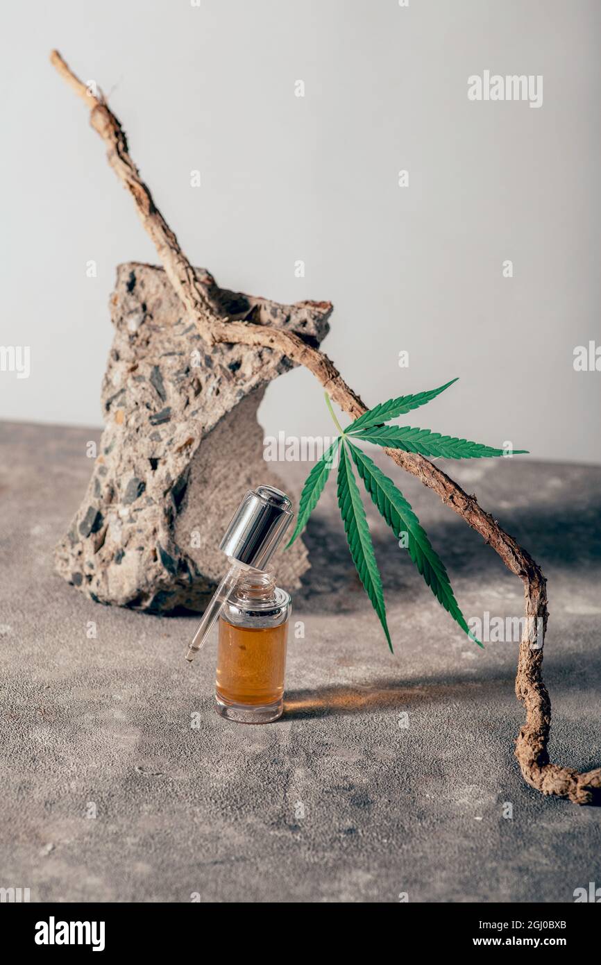 Glass bottle with CBD oil, THC tincture and hemp leaf on gray marble ...