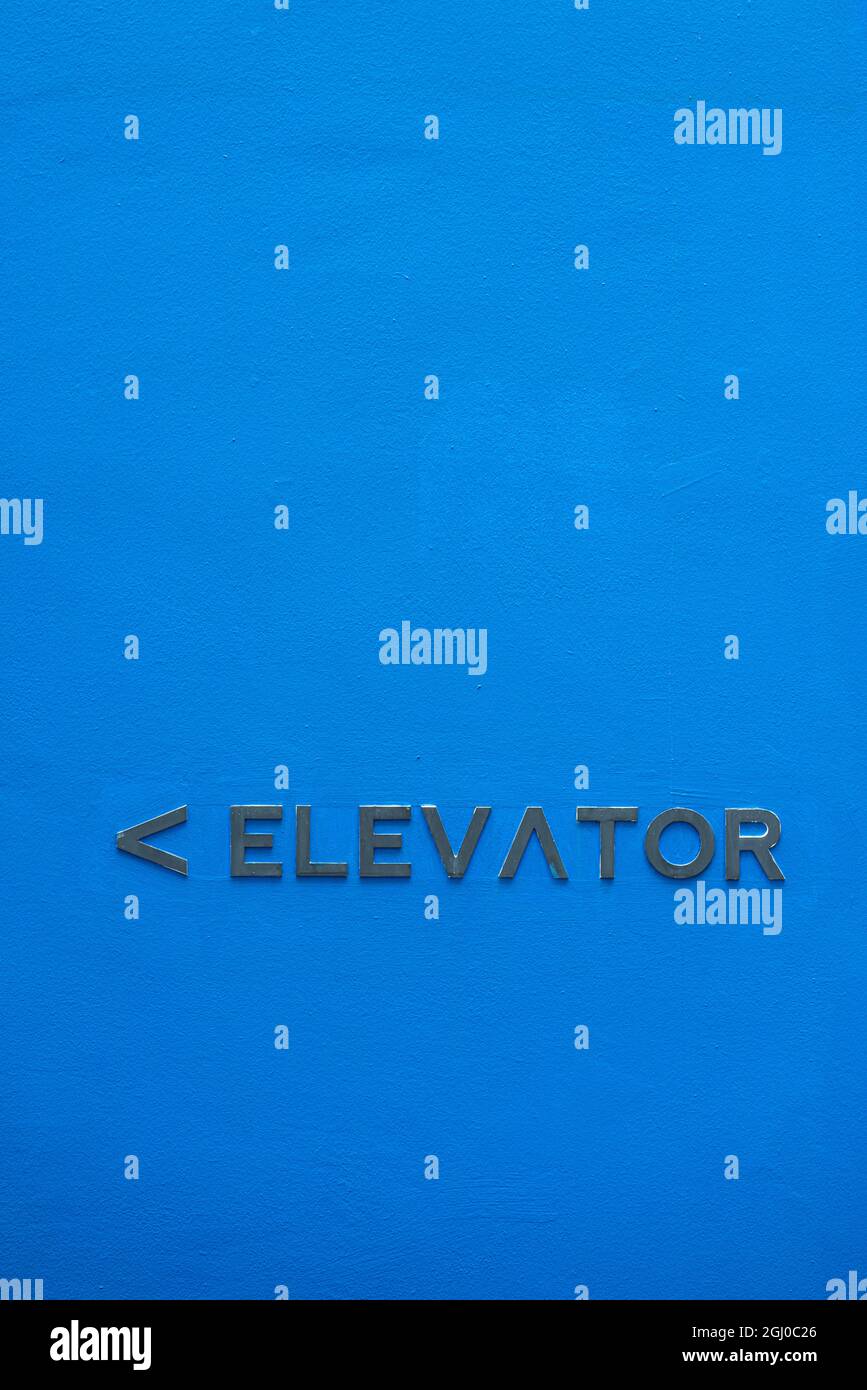 Sign on blue wall indicating the direction to the elevator Stock Photo ...