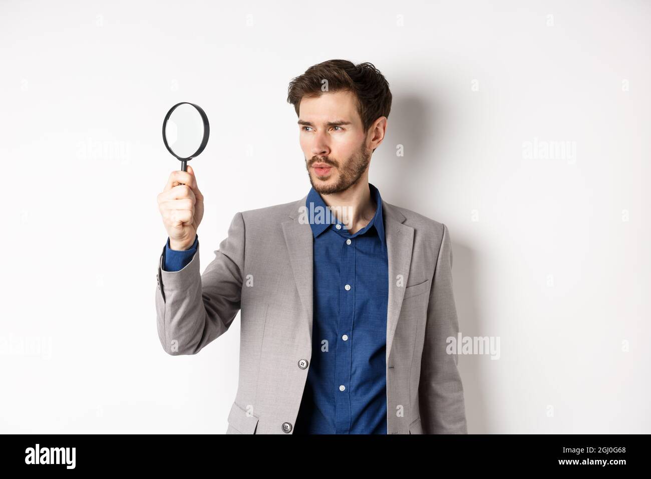 Serious man in suit searching for clues through magnifying glass ...