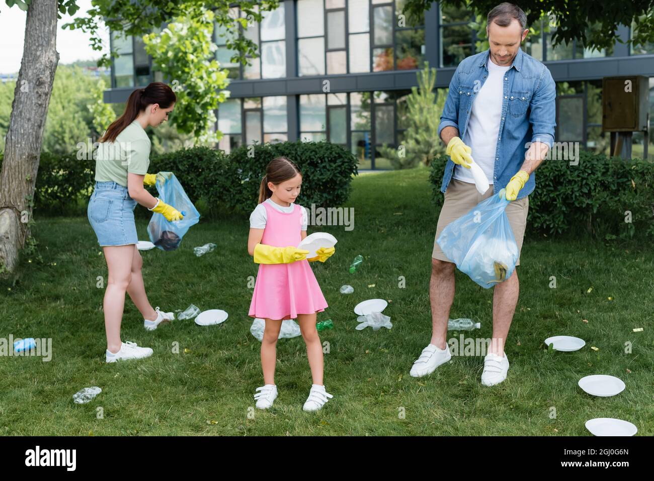 Child holding plastic garbage near parents with trash bags outdoors ...