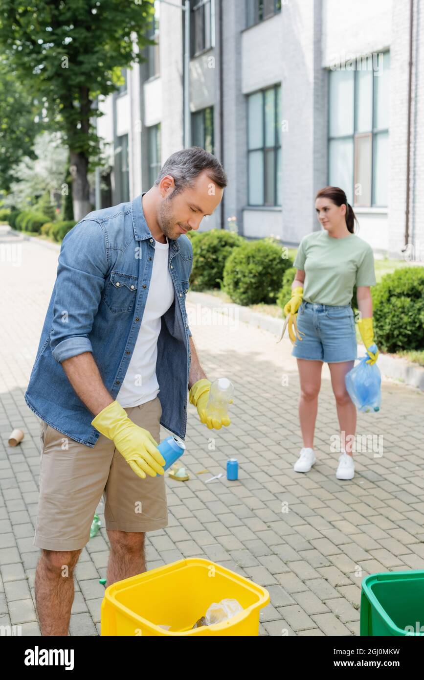 Adult man in rubber gloves sorting trash near cans outdoors Stock Photo ...