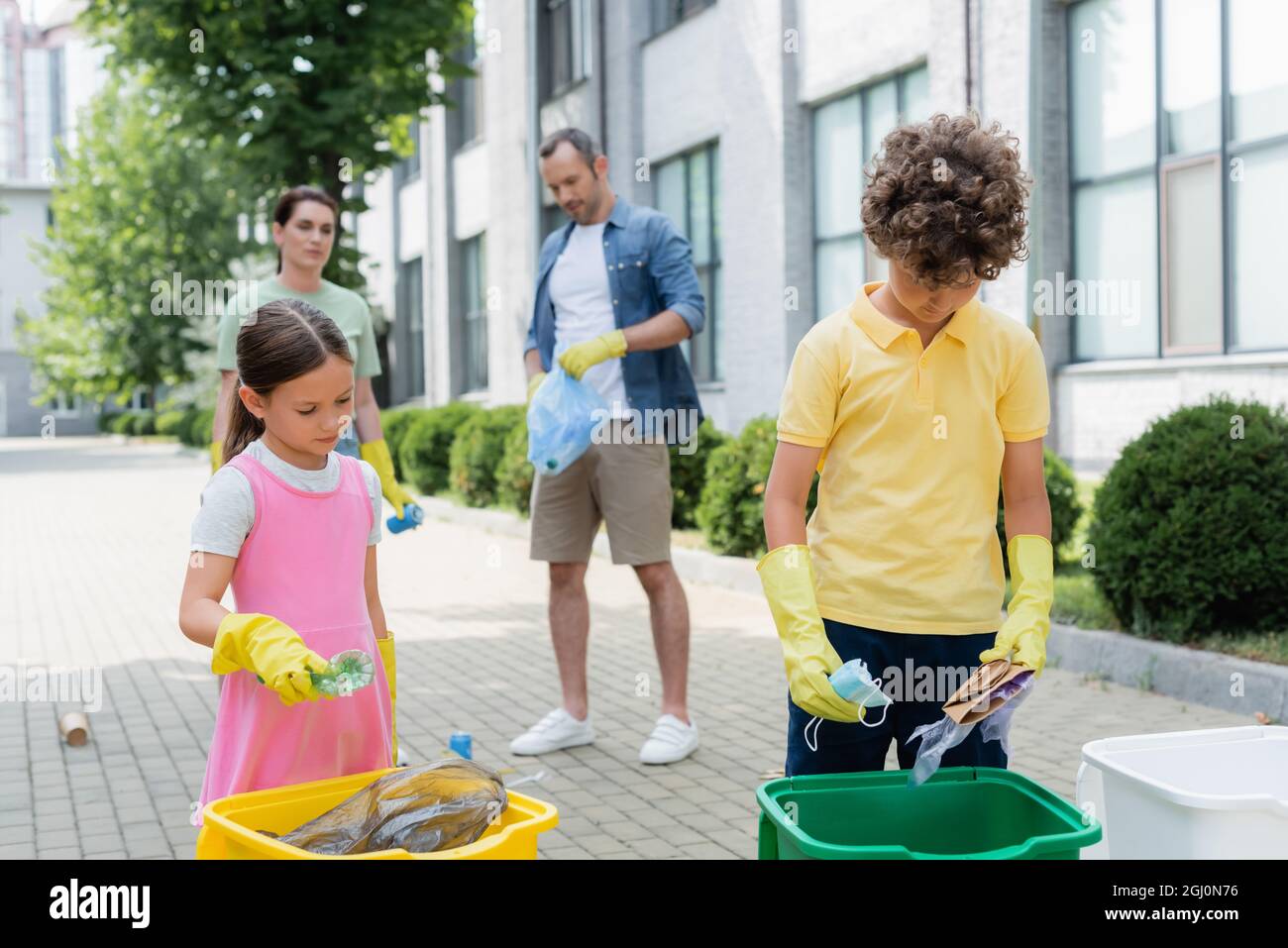 Children holding garbage near cans and blurred parents on urban street ...