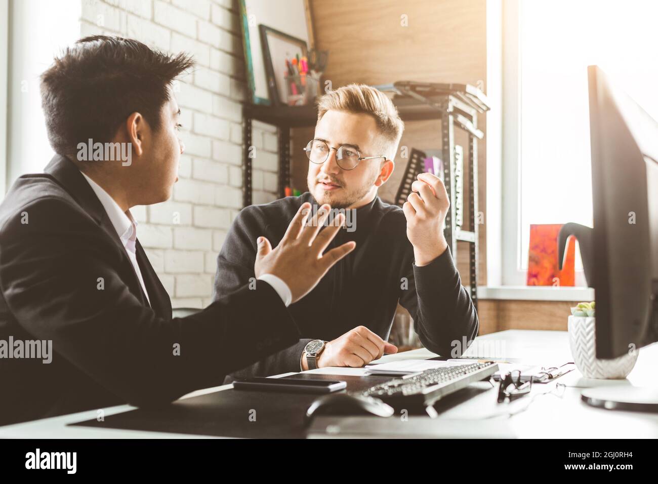 Young office worker sitting at desk, using computer. Two business man ...