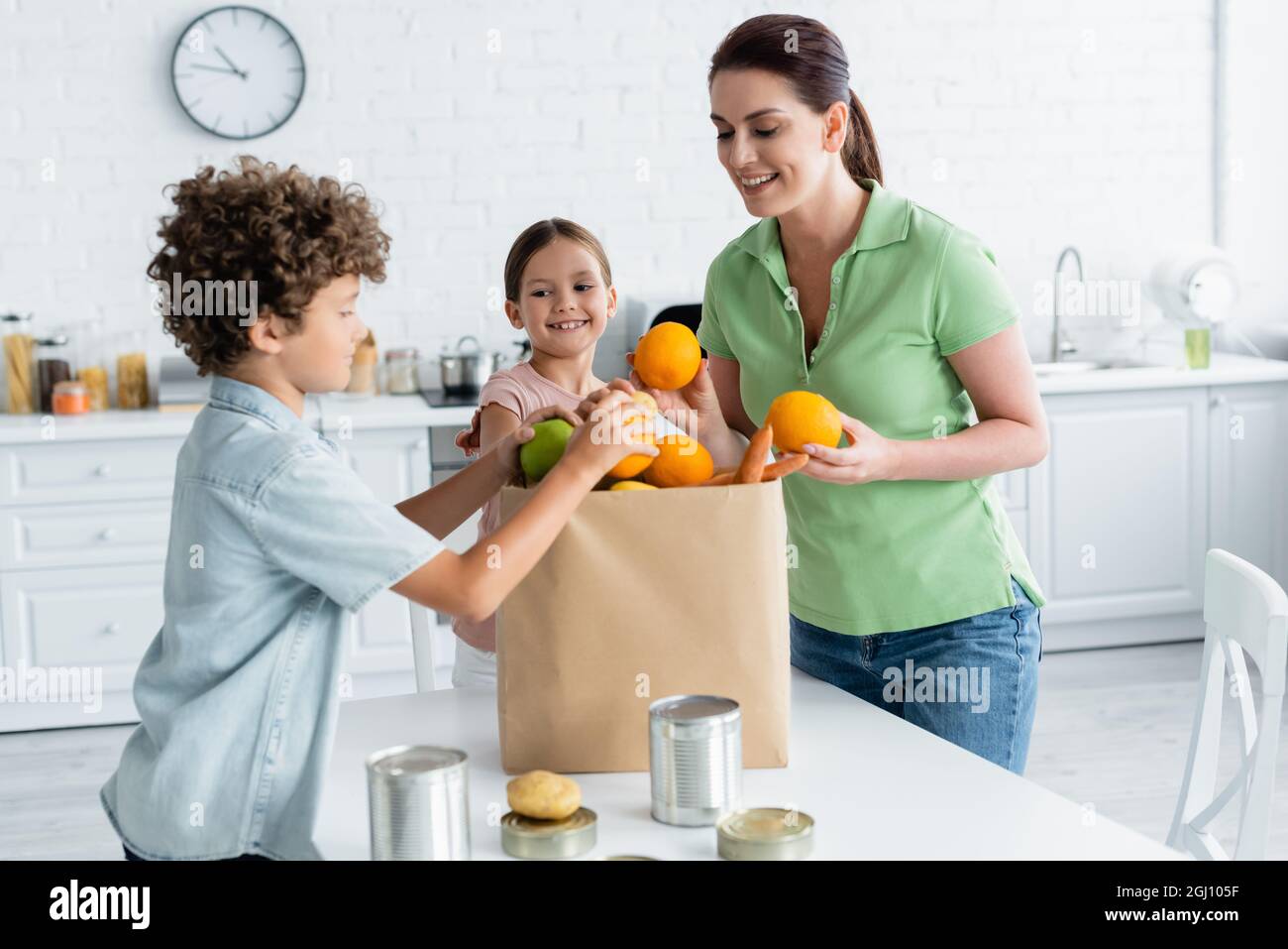 Positive mother and children taking food from paper bag in kitchen ...