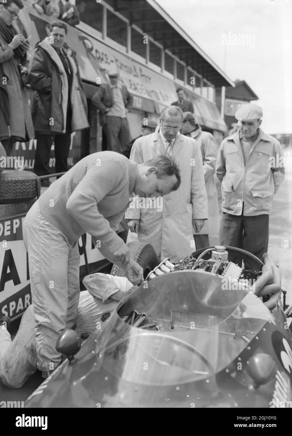 CAR RACING DRIVER JOHN SURTEES WORKS ON HIS CAR BEFORE THE RACE AT ...