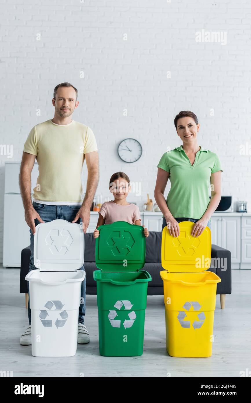 Positive family with daughter standing near trash bins with recycle ...