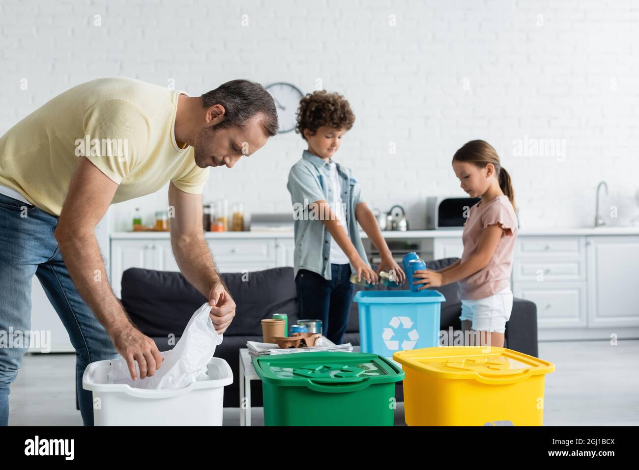 Man sorting garbage near blurred kids and trash cans with recycle sign ...