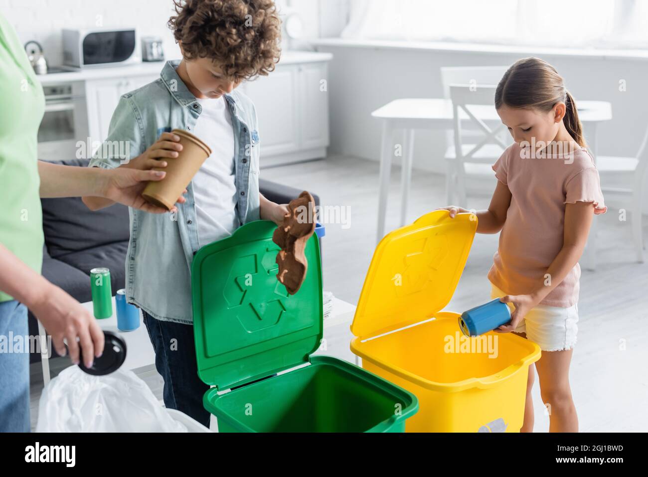 Kids sorting garbage near mother and trash cans with recycle sign at ...