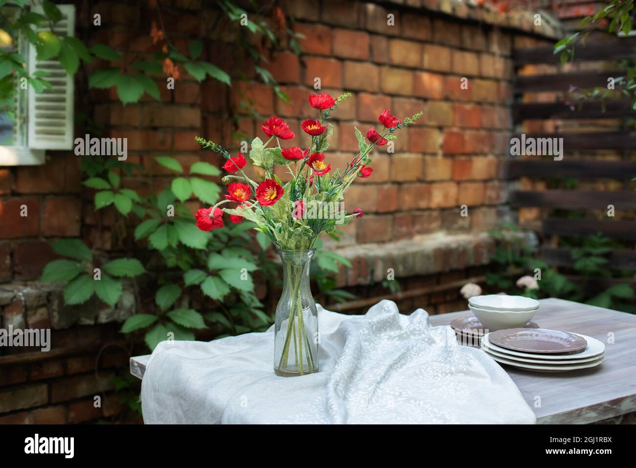 bouquet poppies in vase. Interior Terrace. Wooden table and plates for ...