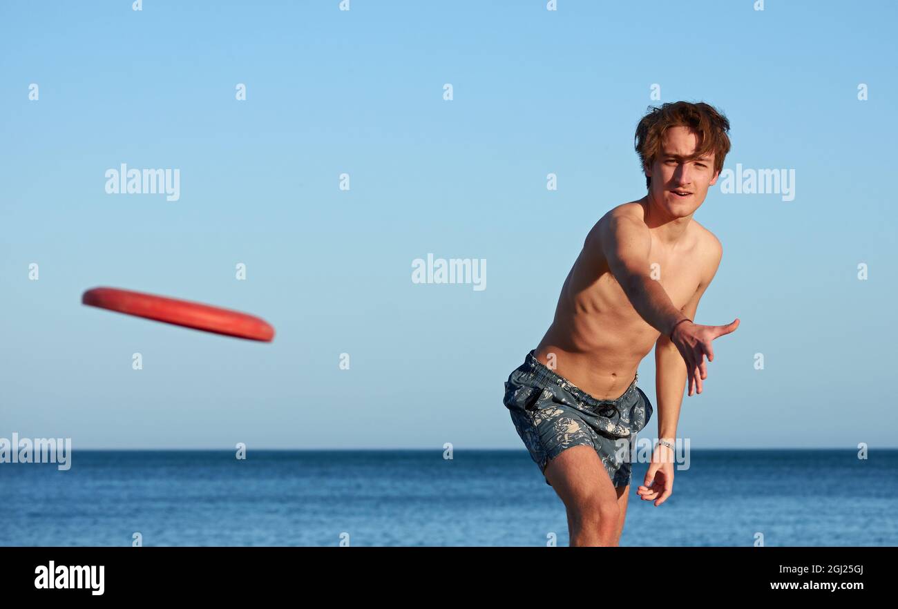 Young fit caucasian male throwing a frisbee and having fun on the beach ...