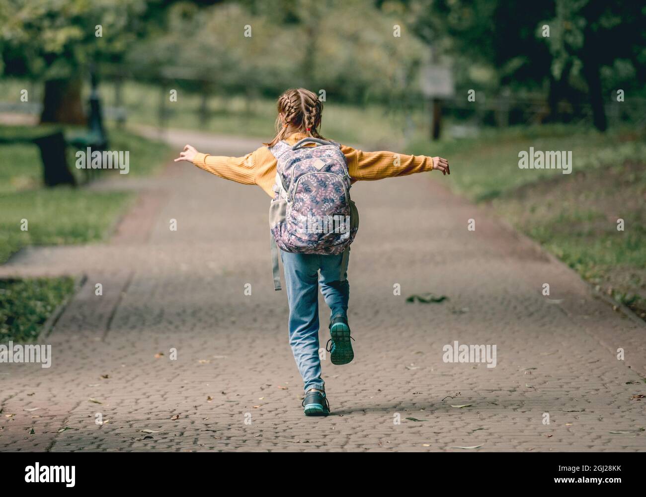Preteen school girl with backpack running in the park after lessons ...