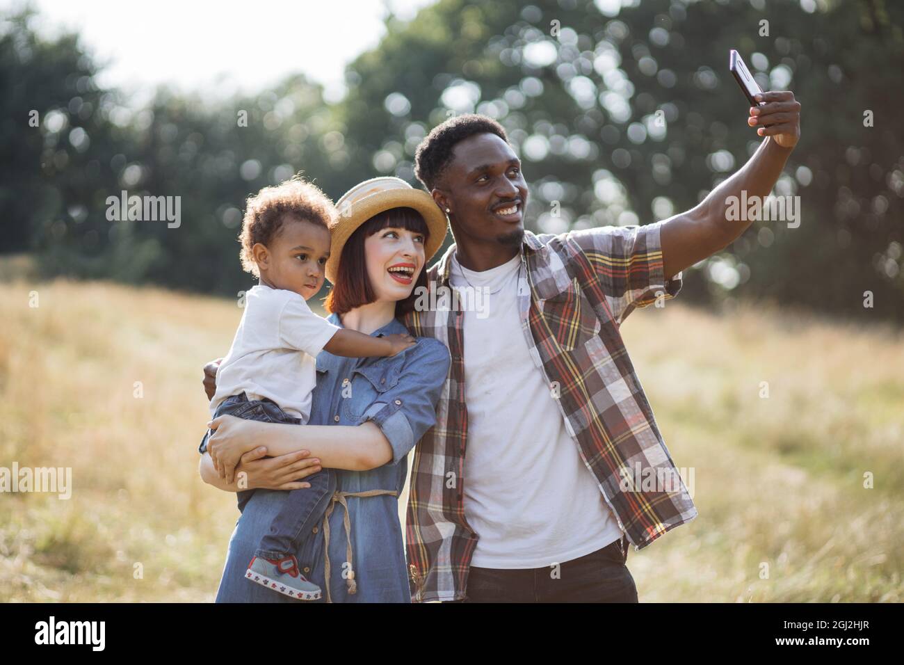 Happy young parents with little son on hands standing summer field and ...