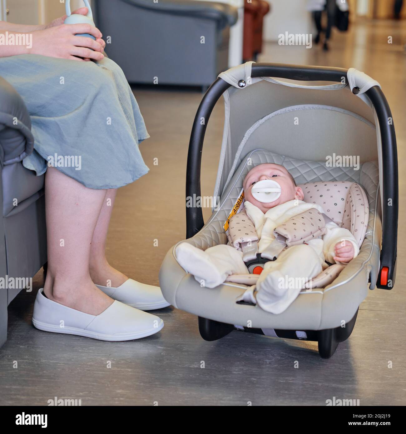 A mother with a newborn baby in a carrier is waiting for a doctor ...