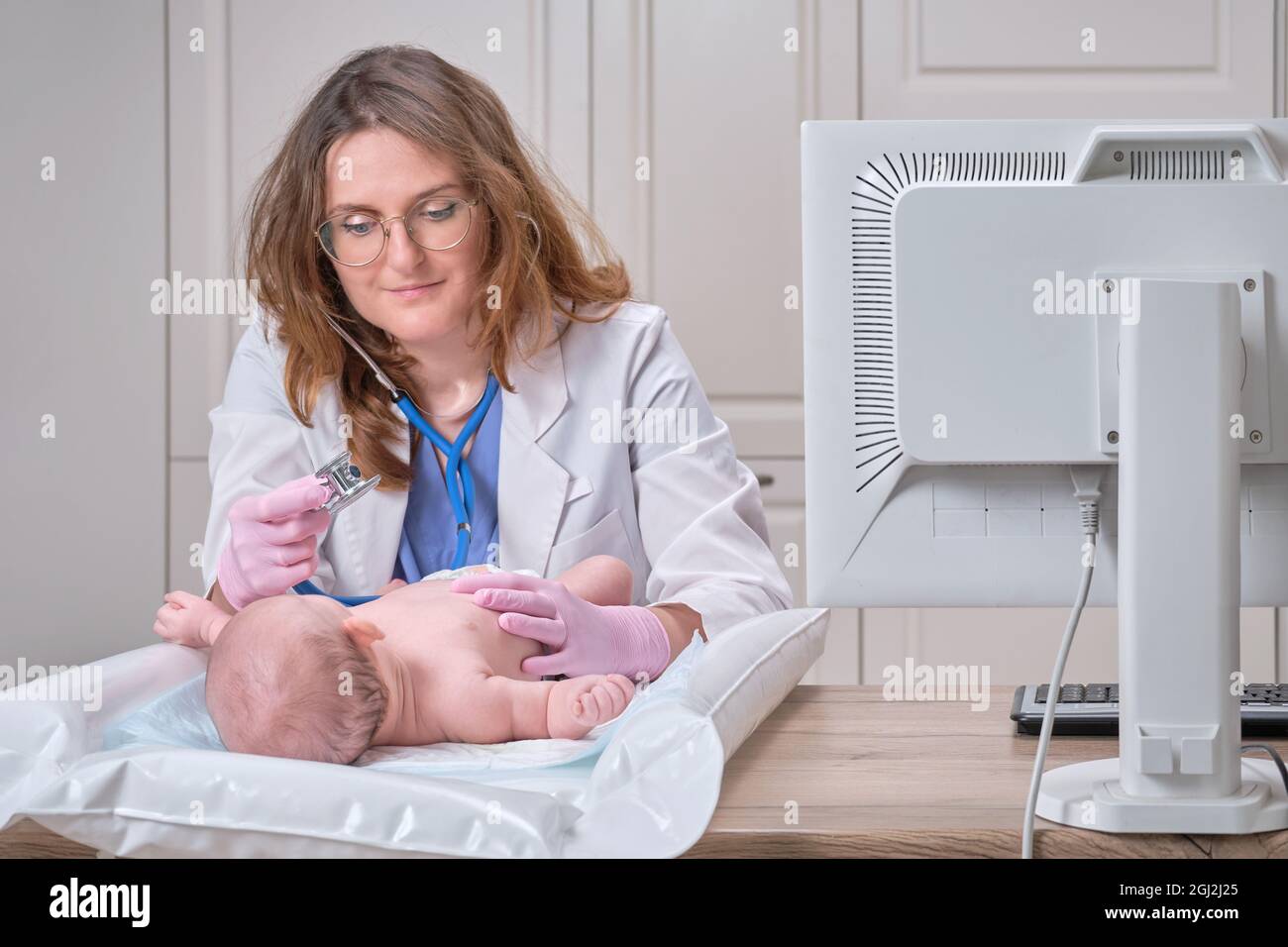 Woman doctor listens with a stethoscope to a newborn baby. Nurse checks ...