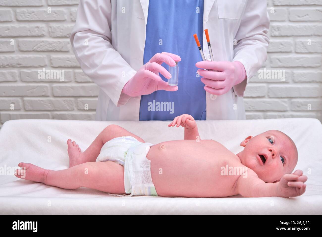 The doctor uses a syringe to inject a newborn child. A nurse in uniform ...