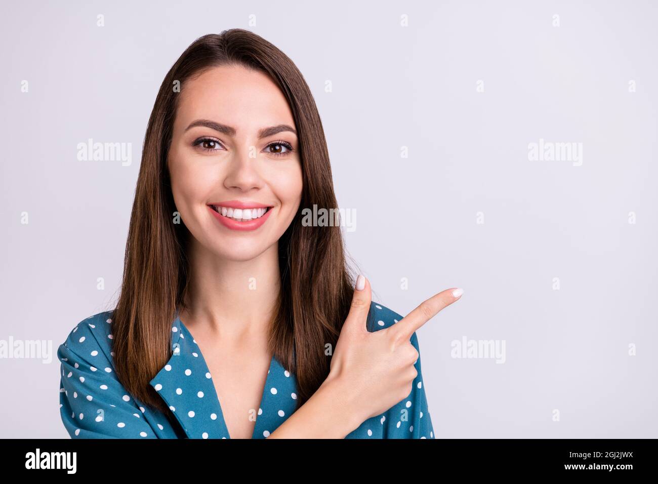 Photo of sweet shiny young lady wear dotted shirt pointing finger empty ...