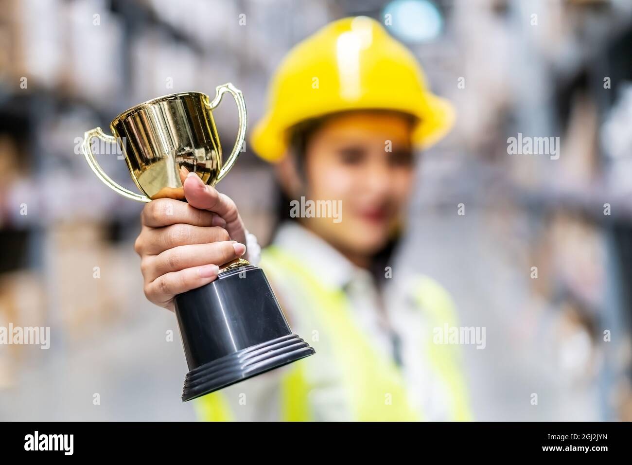 Happy woman warehouse worker holding a trophy after being selected as ...