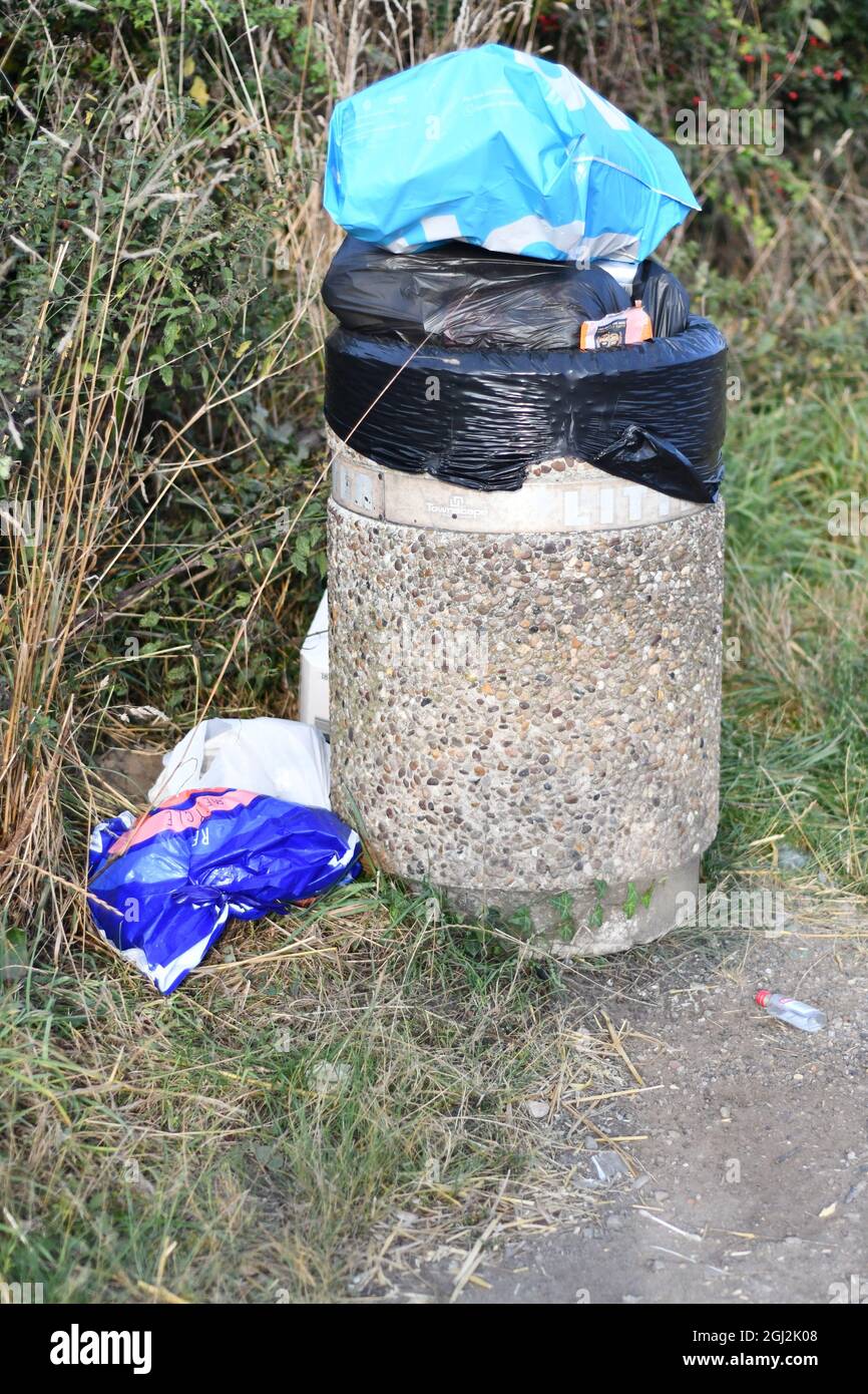A pebble dashed rural waste bin overflowing with plastic bags full of ...