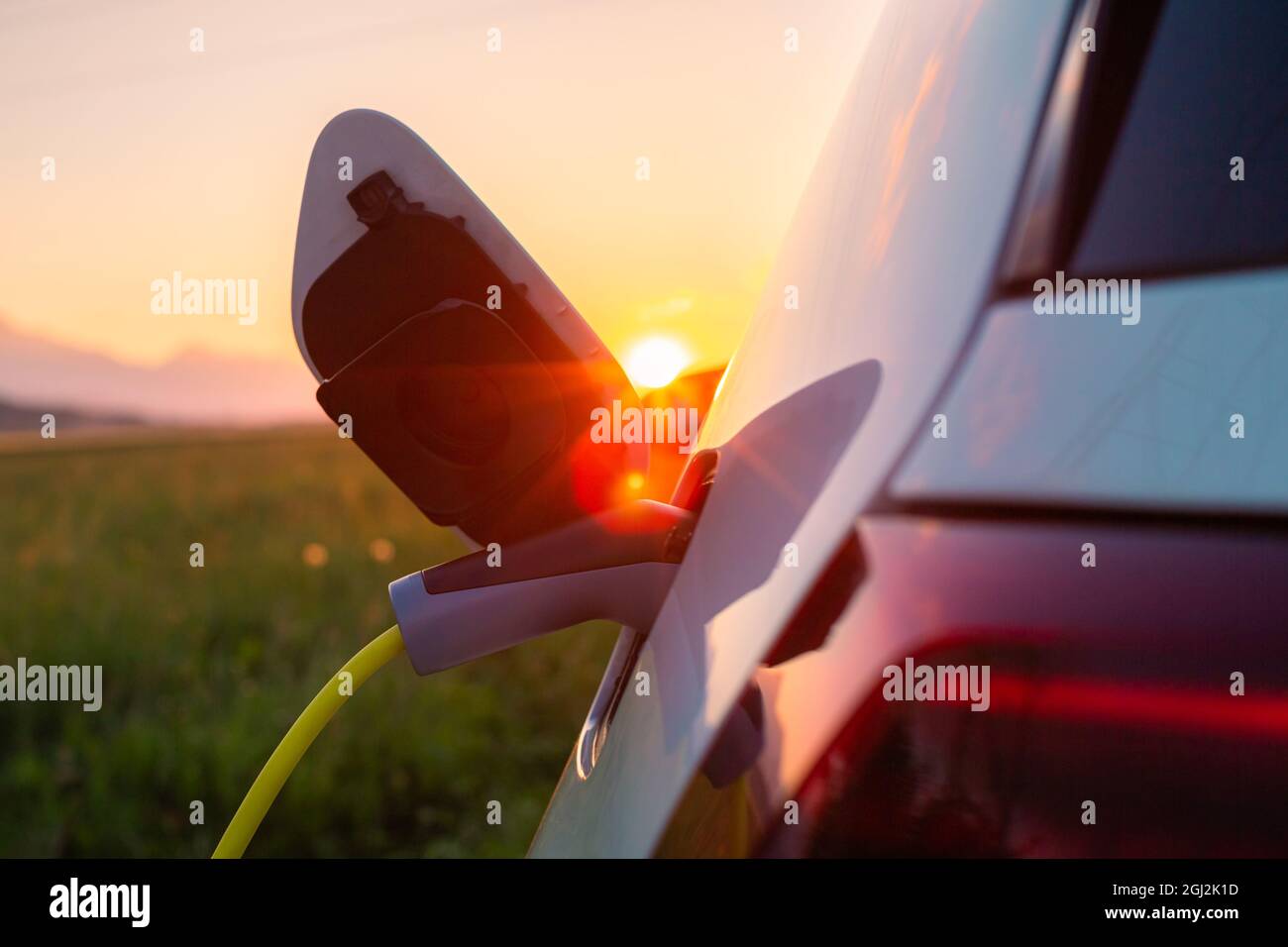 Electric car with opened charging socket cap and charger plugged in, at ...