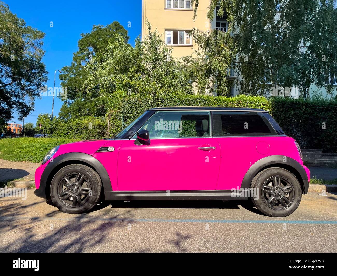 Side view of a bright pink mini car parked in the street with a house ...