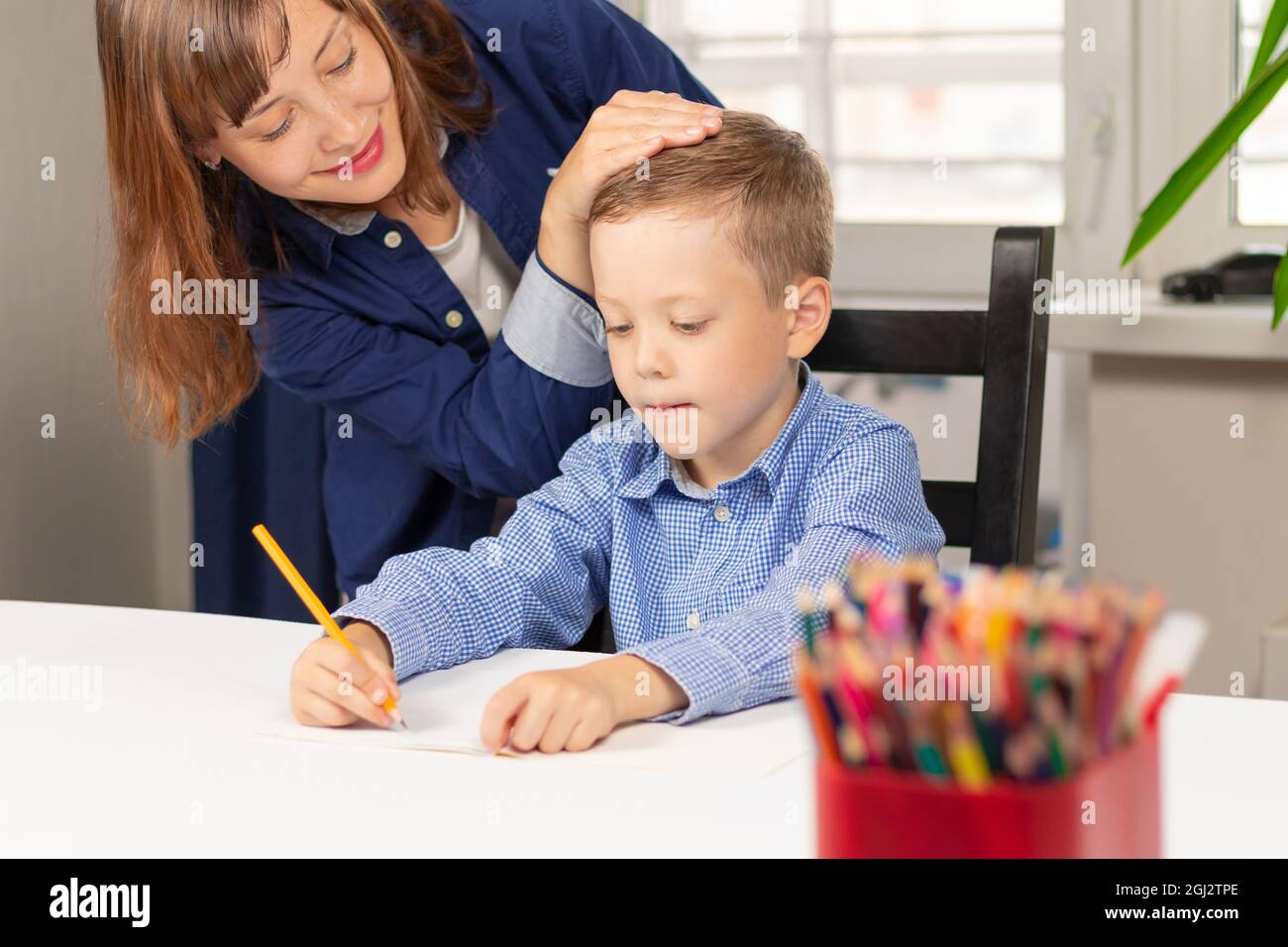 Cute seven year old baby boy doing homework at home with mom on a white ...