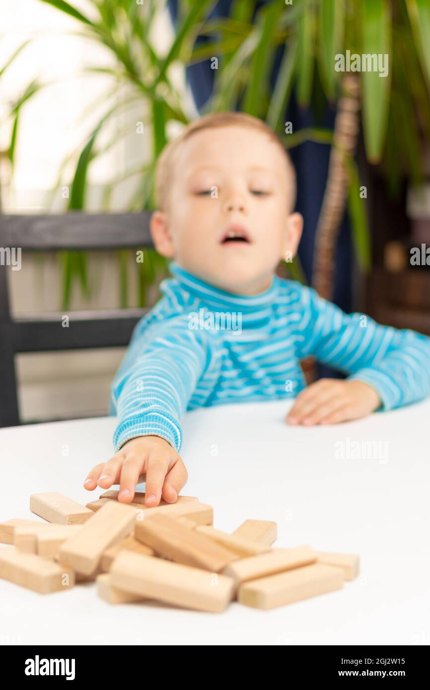 A cute seven-year-old child boy playing Jenga at home at a white wooden ...