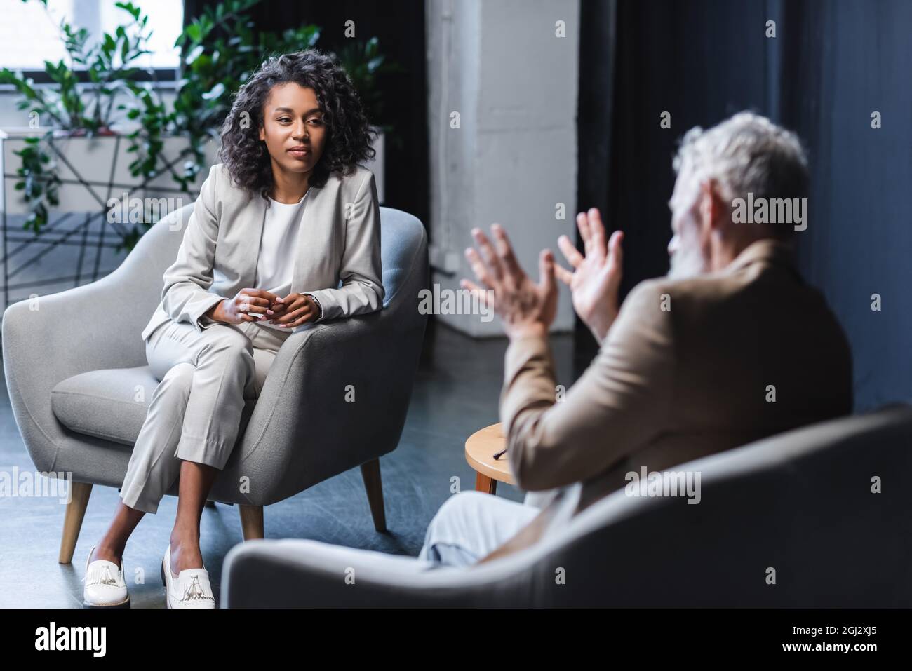 curly african american journalist looking at blurred businessman ...