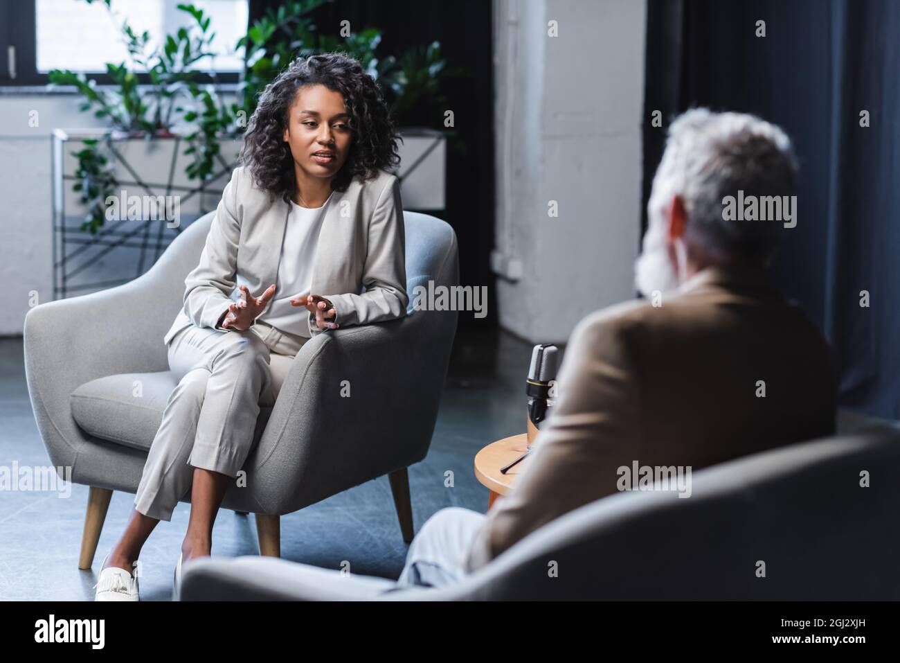 curly african american journalist gesturing while talking with blurred ...