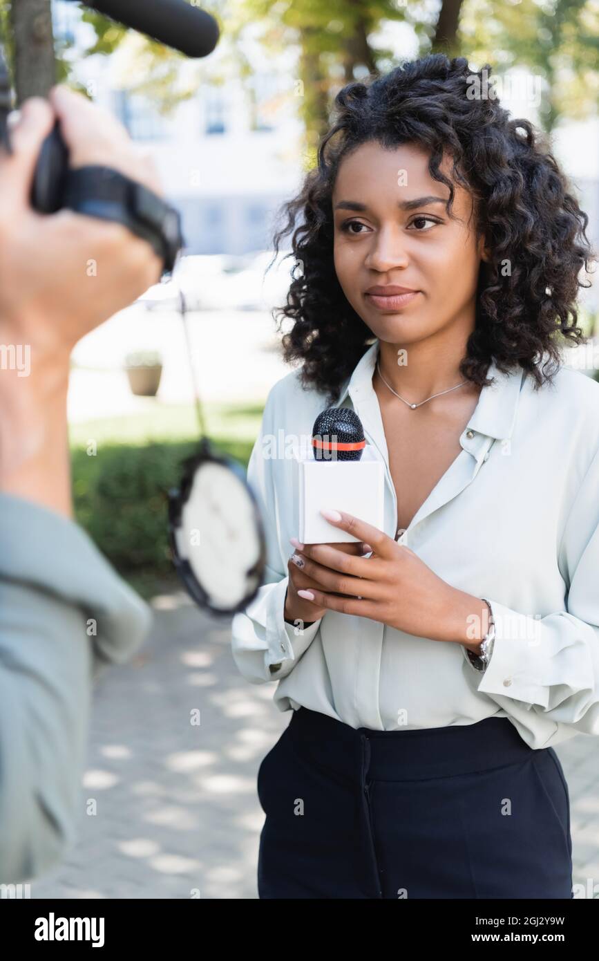pretty african american journalist with microphone doing reportage near ...
