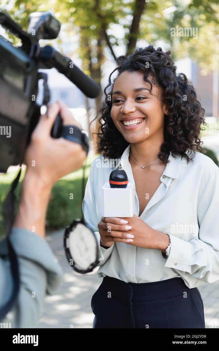 smiling african american journalist with microphone doing reportage ...