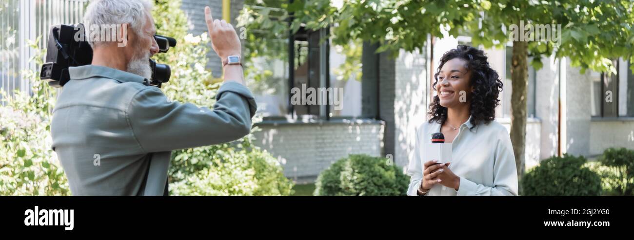 cameraman pointing with finger near happy african american reporter ...