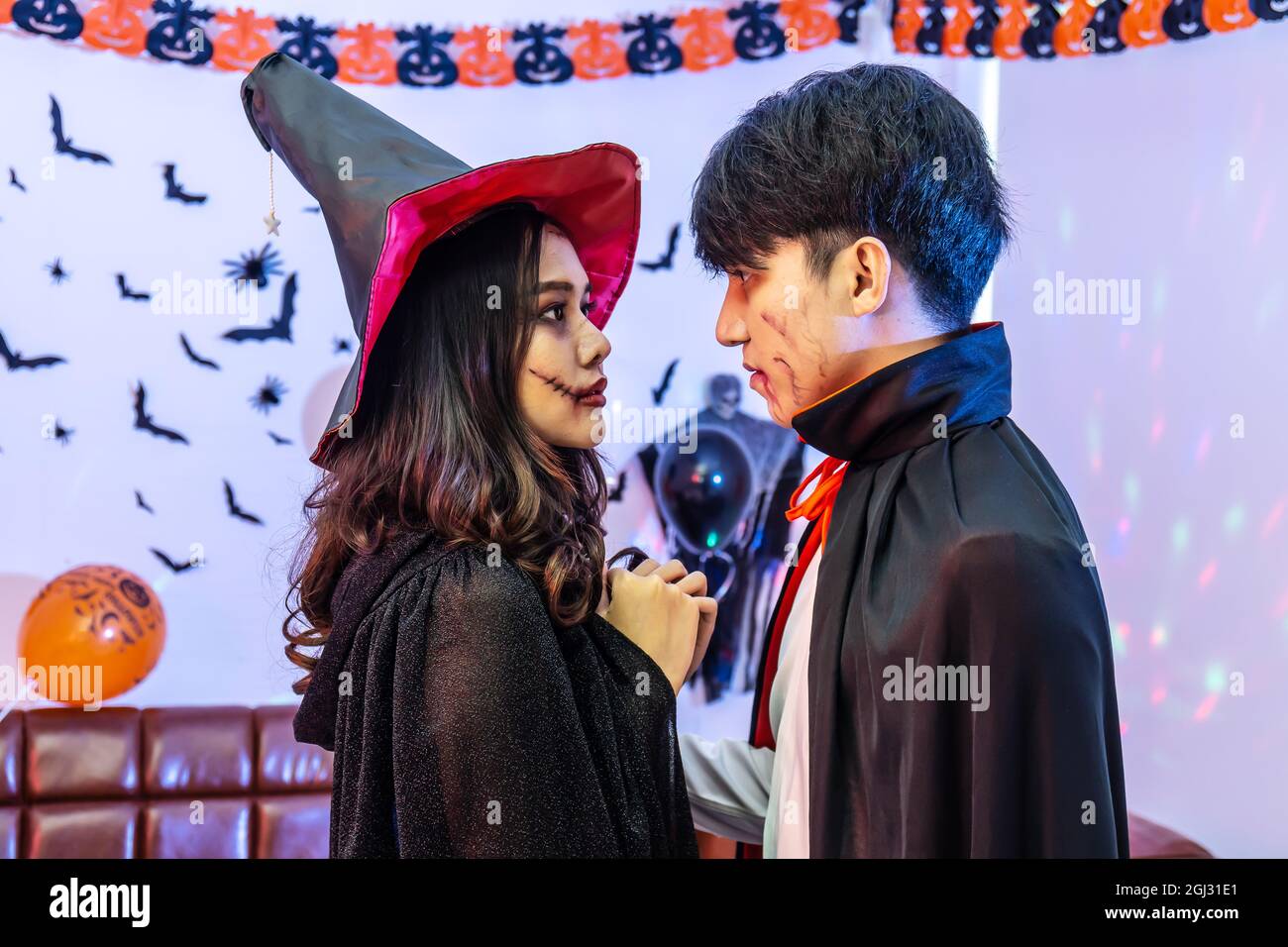 Halloween loving couple vampire in cloak and witch girl looking at each ...