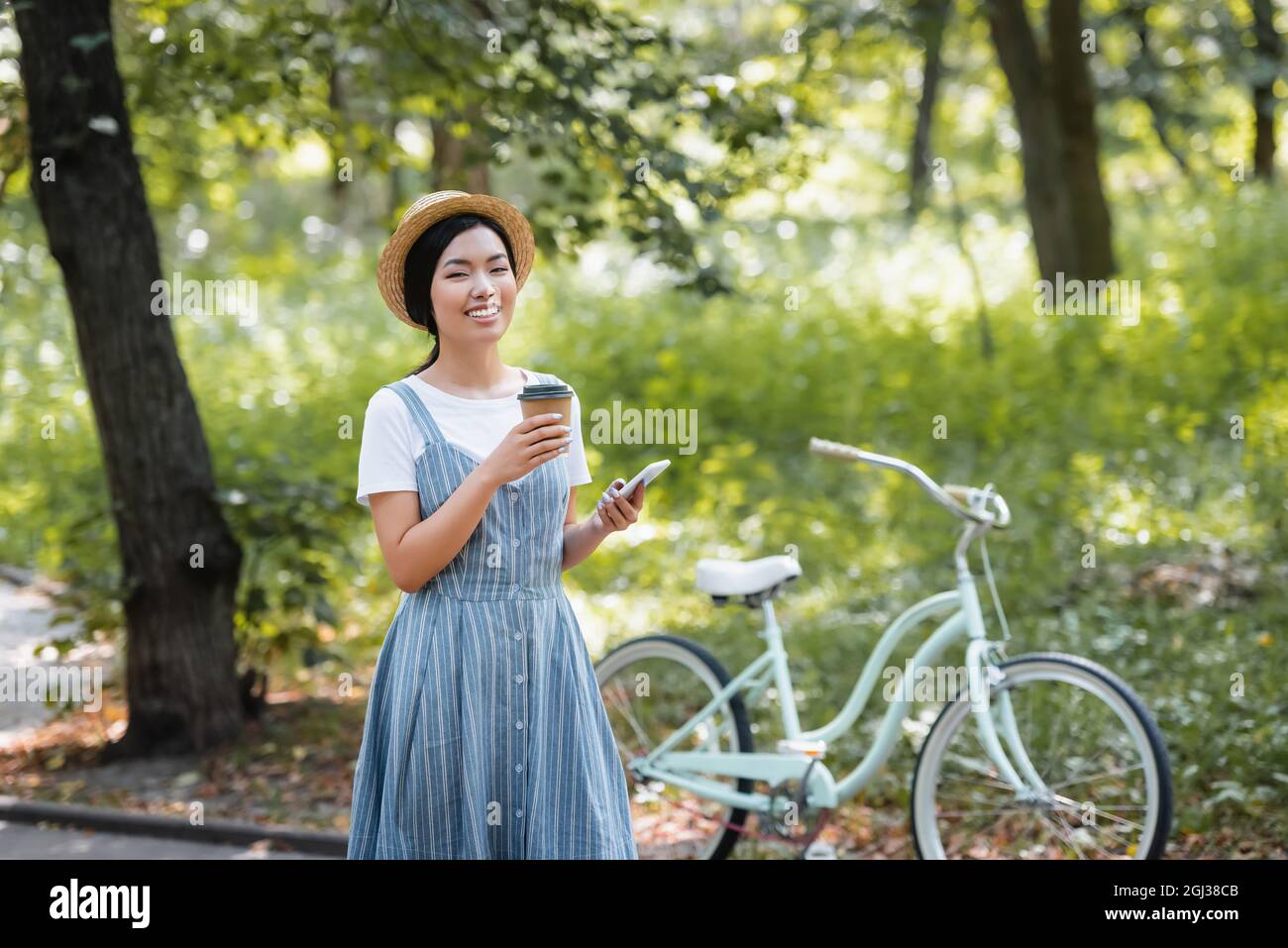 happy asian woman with takeaway drink and mobile phone looking at camera near bike in park Stock ...